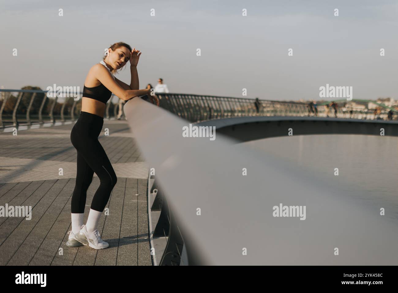 A fit young woman in athletic attire leans on a sleek railing ...