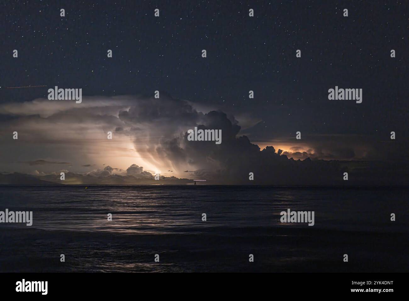 Thunderstorm cell over the sea at night with visible stars in the sky ...