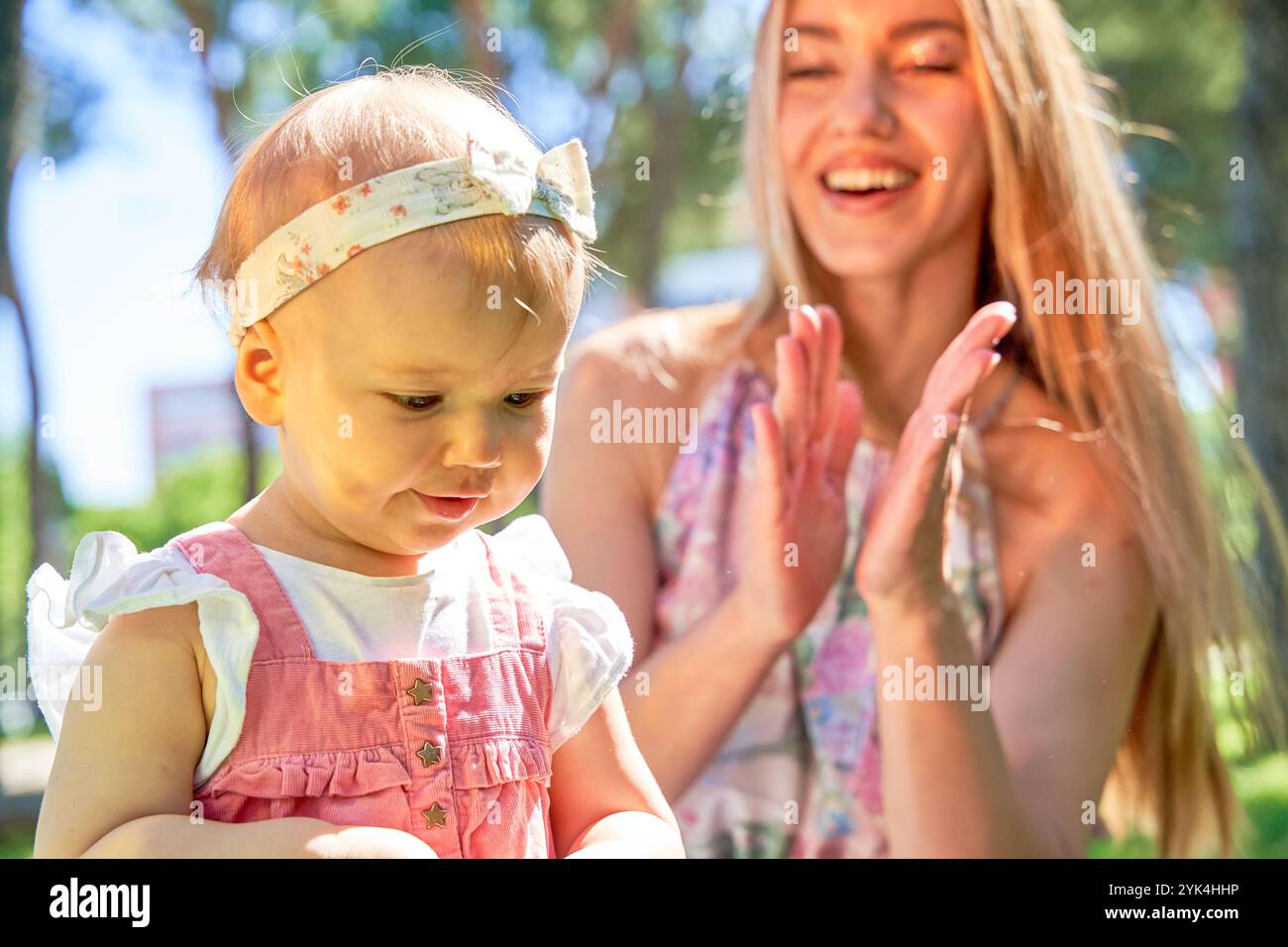 Baby girl in a pink dress exploring the park, with her mother clapping ...