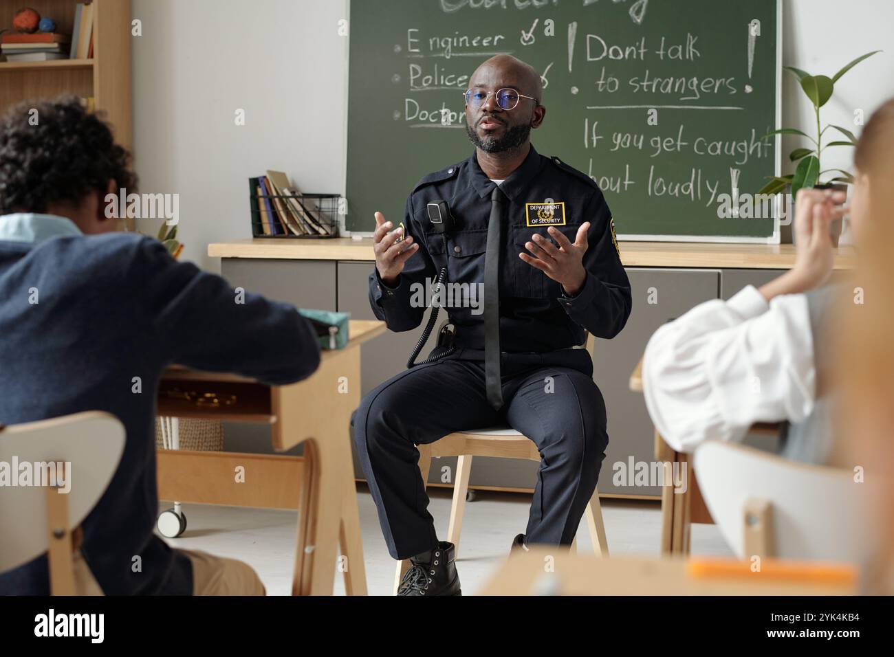 Young confident security guard in uniform sitting in front of diligent ...