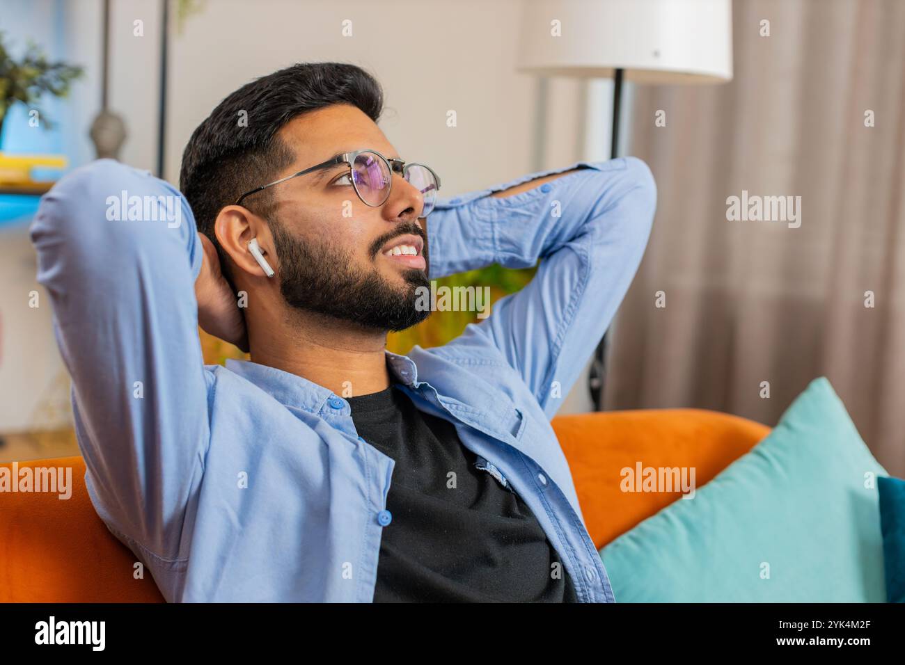 Happy relaxed young Indian man resting on couch with wireless earphones ...