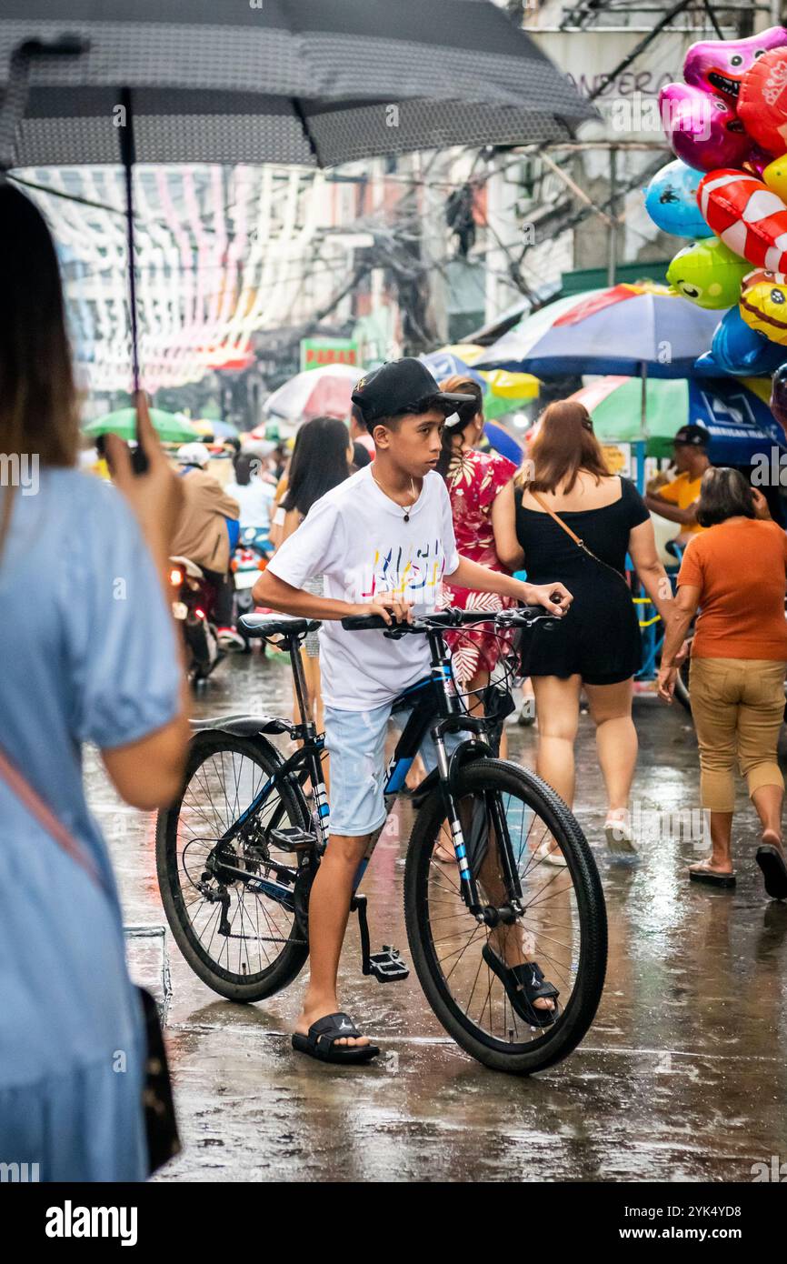 A young Filipino boy makes his way along a busy market street riding his bicycle in The Tondo ...