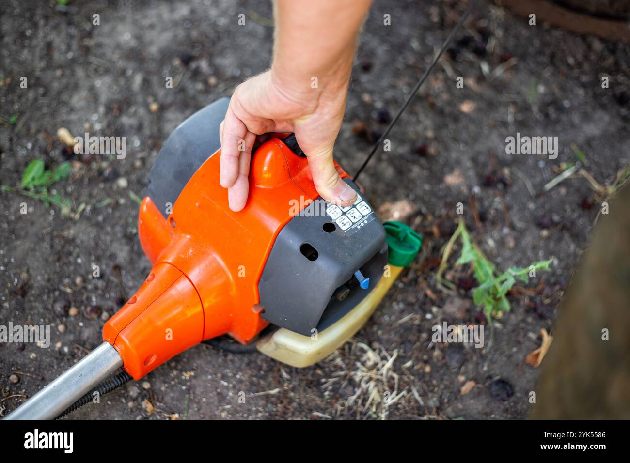 Starting a gas mower to cut grass. A man pulls the recoil starter to ...