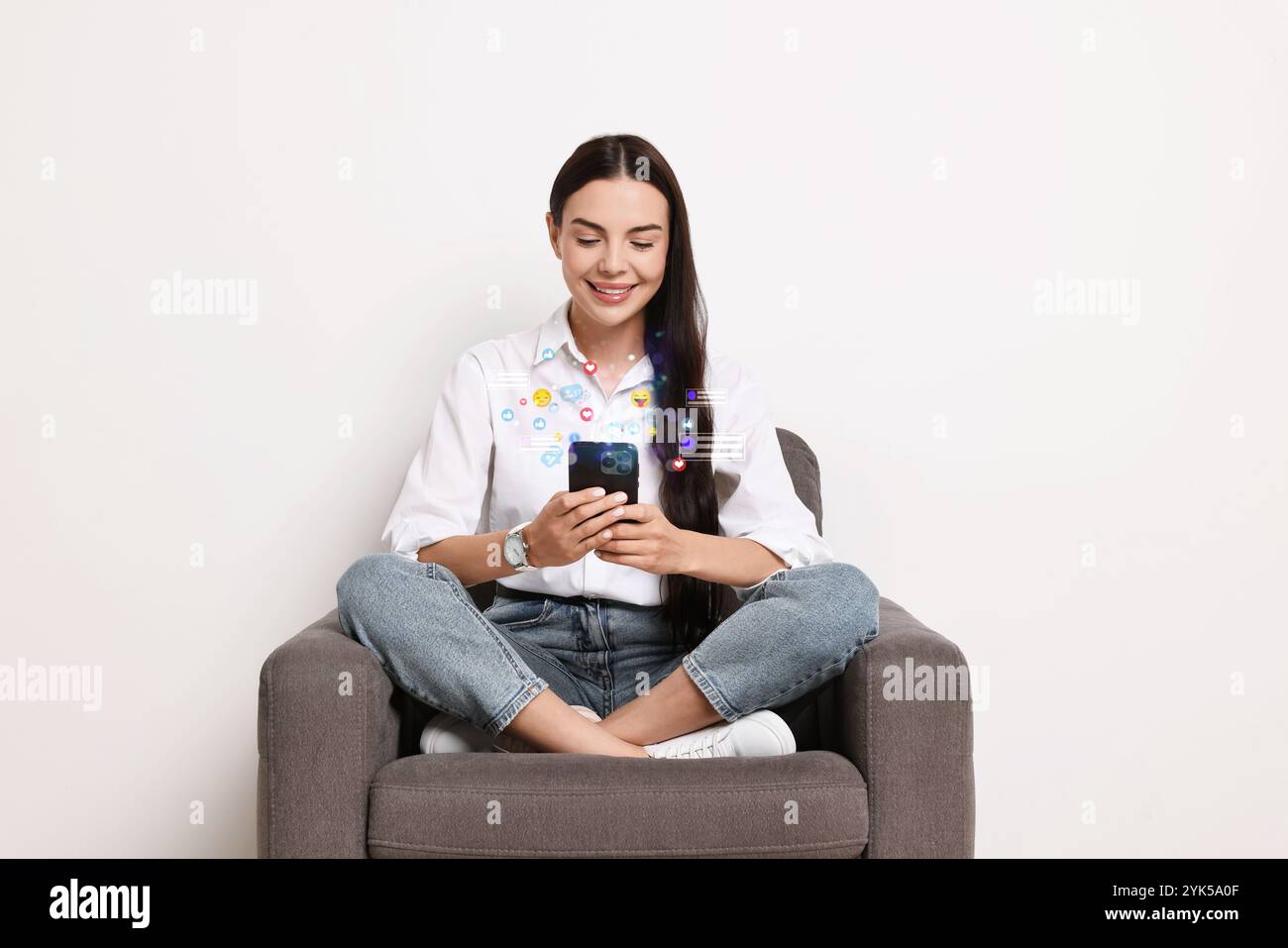 Happy woman using mobile phone while sitting in armchair on white ...