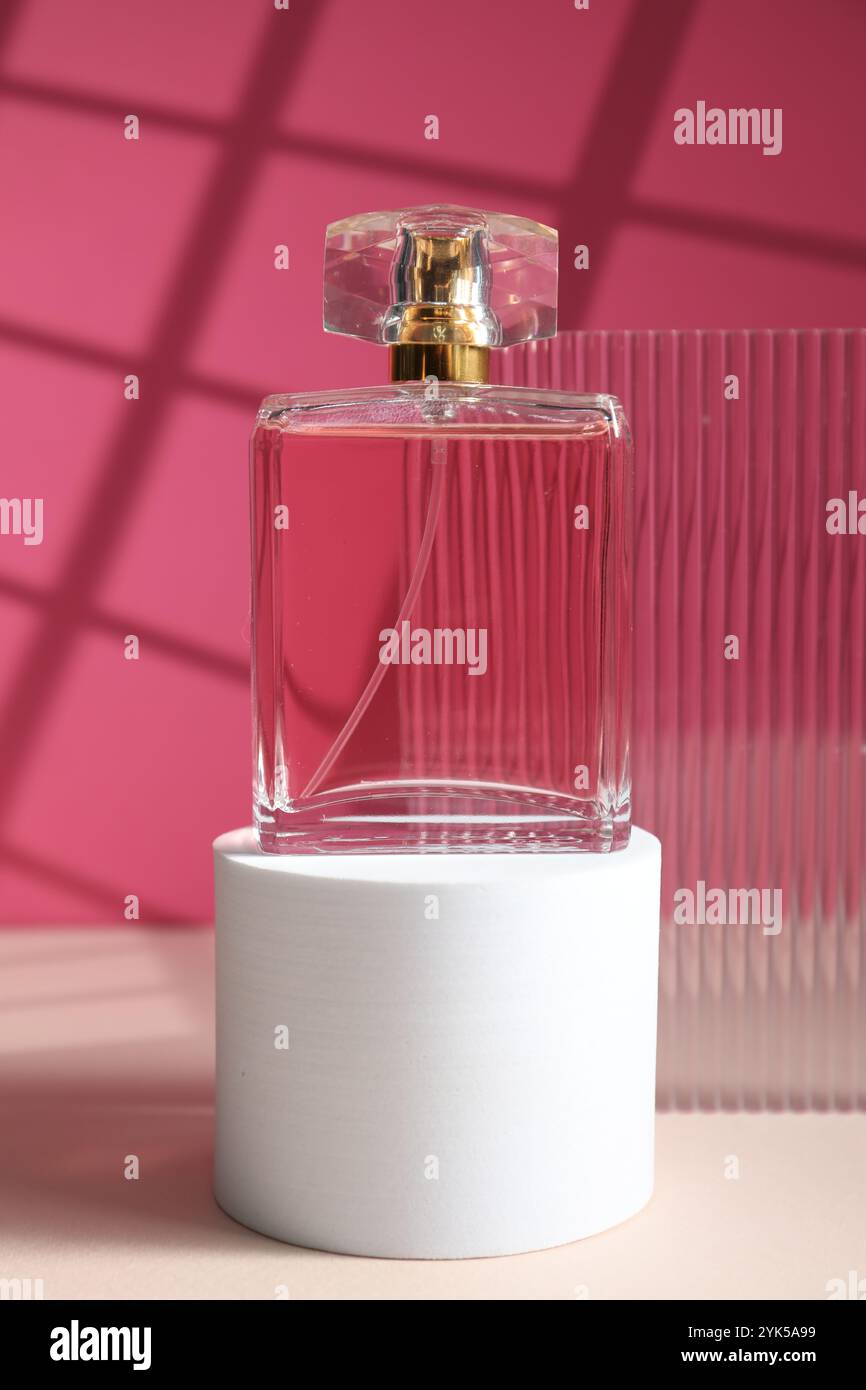 Stylish presentation of perfume bottle on white table against pink ...