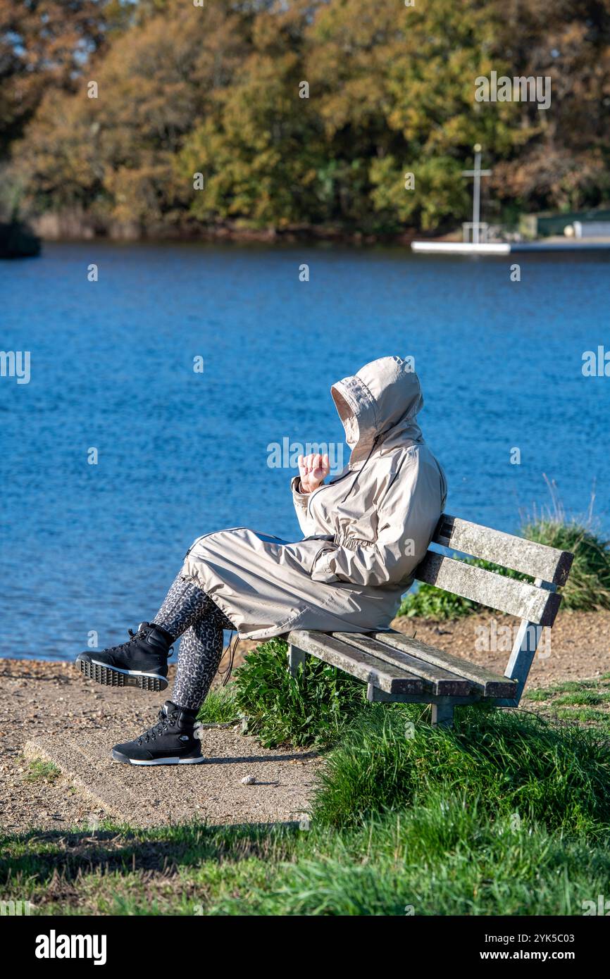 mysterious lady sitting on a wooden bench wearing a long raincoat with ...