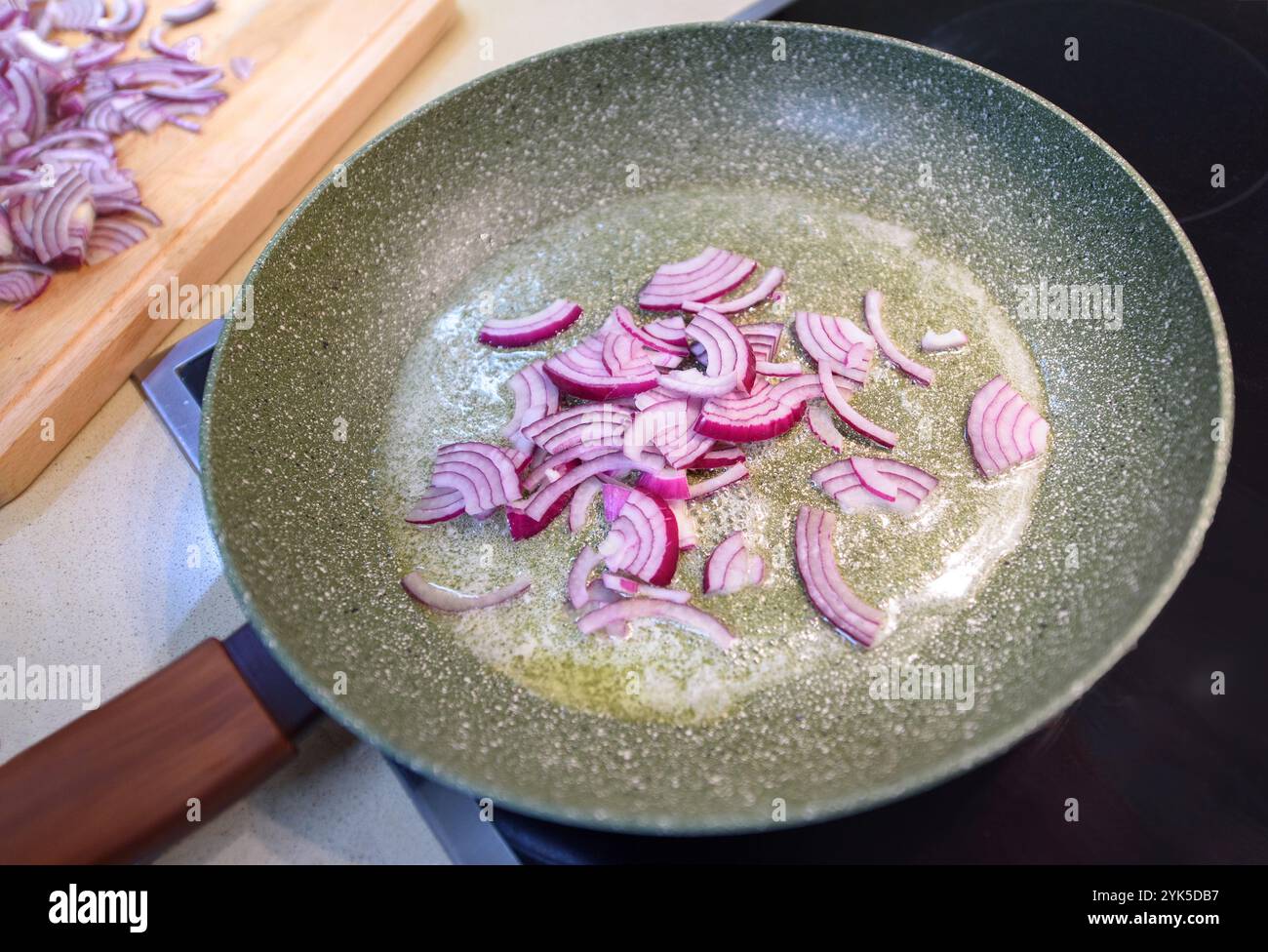 Sliced red onions are sauting in a skillet with oil, creating a ...