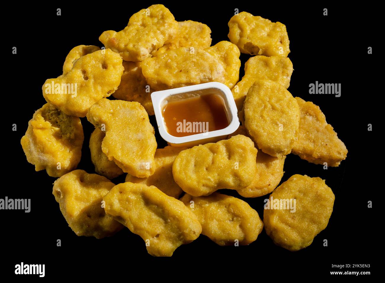 A tray of golden colored chicken nuggets sits on a black background ...