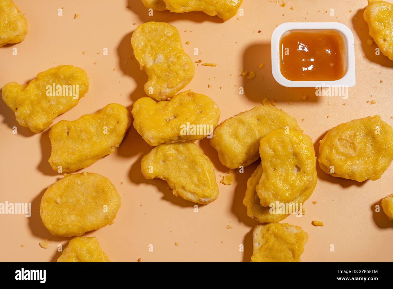 A tray of golden yellow chicken nuggets sits on a table. A small white ...