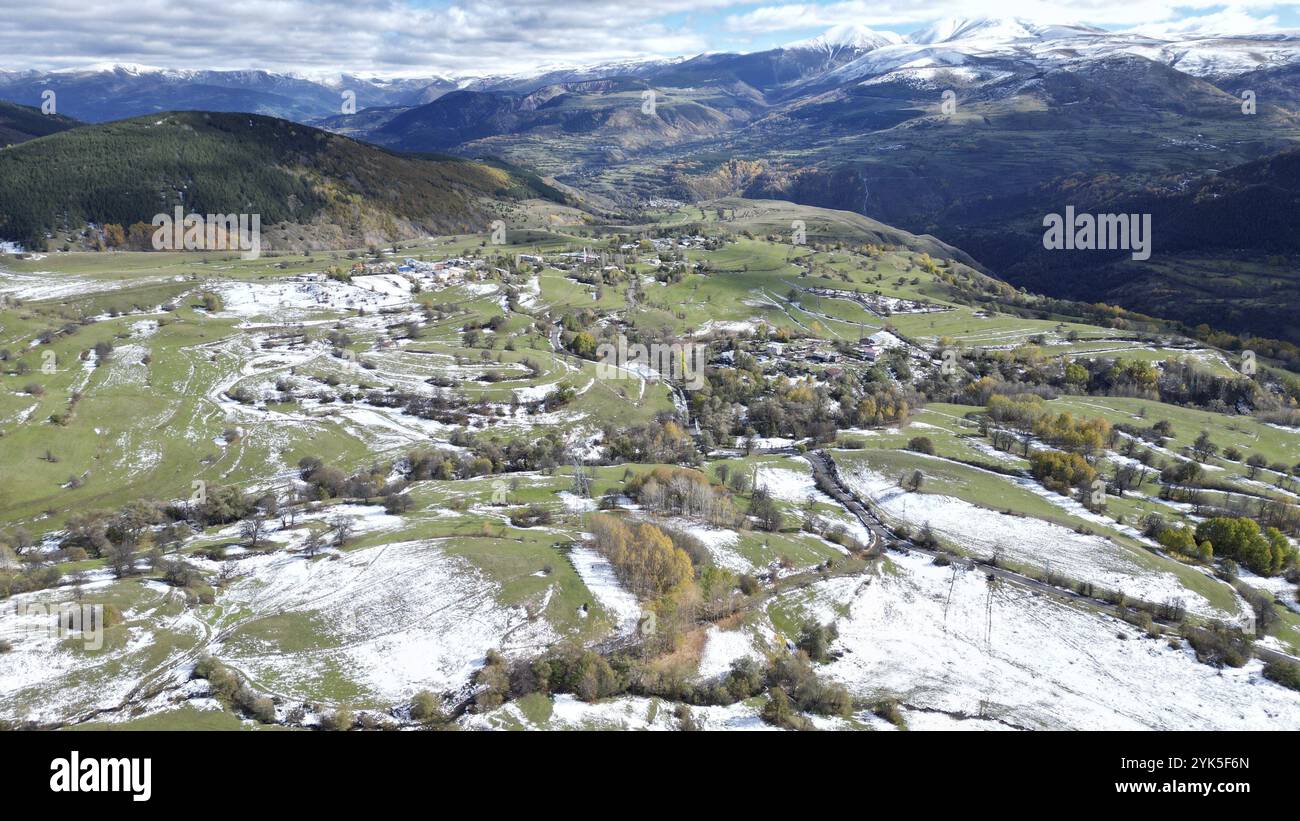 Aerial view of snow-patched fields surrounded by mountains and clouds ...