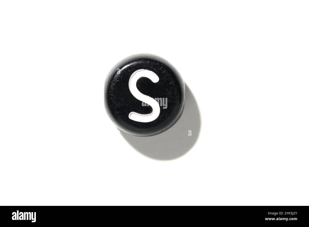 Black round salt shaker with white letter s casting shadow on a white ...