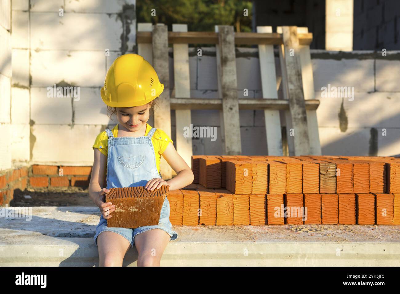 Little girl in a yellow hardhat is playing builder on the construction ...