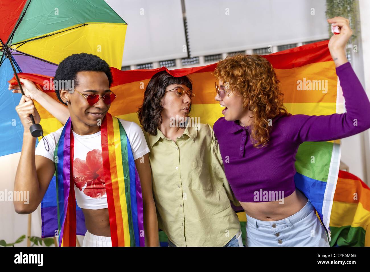Non binary and transgender people dancing waving rainbow lgbt flag celebrating a party at home ...
