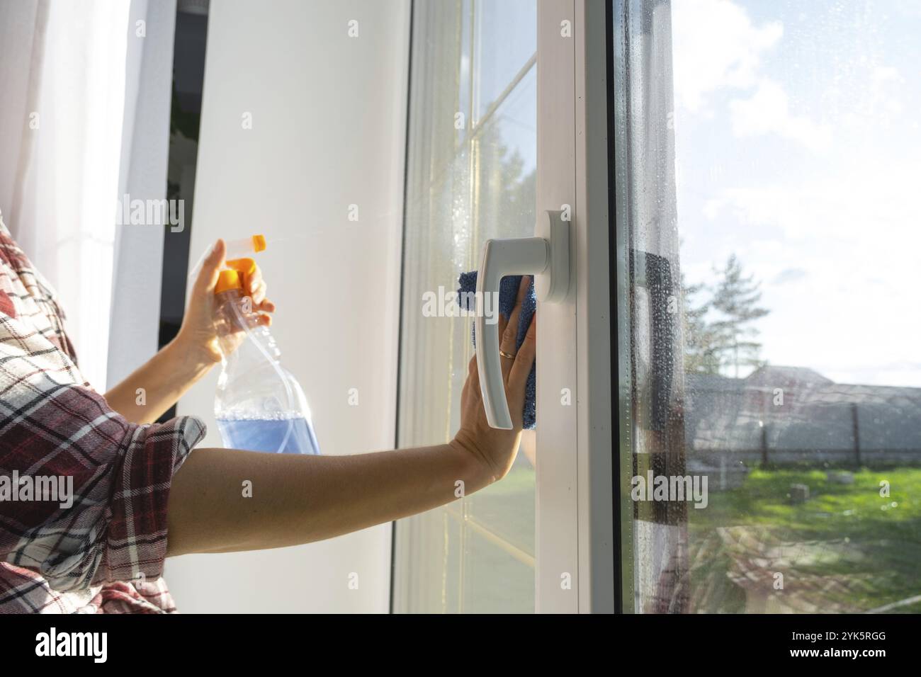 Woman manually washes the window of the house with a rag with spray ...