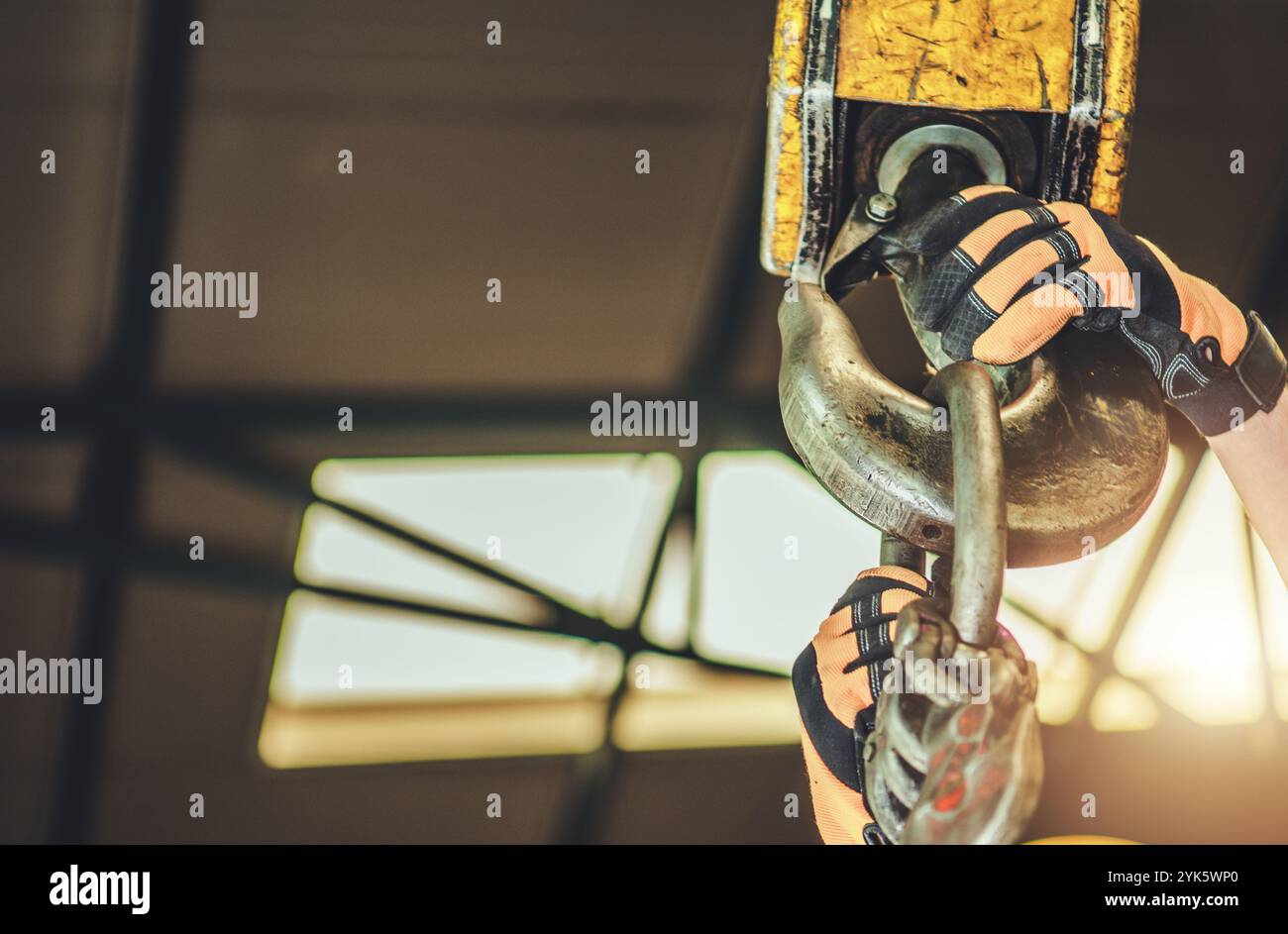 A worker grips a heavy lifting hook in a bright industrial warehouse ...