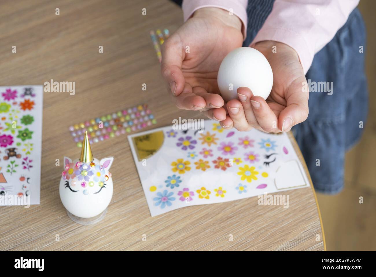 A cute girl with pink bunny ears makes an Easter craft, decorates an ...