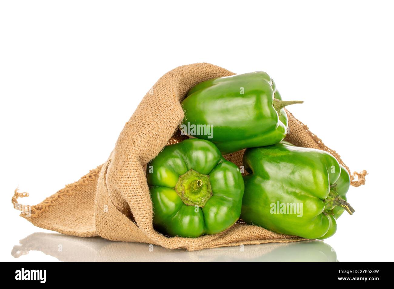 Three sweet green peppers in a jute bag, close-up, isolated on a white ...