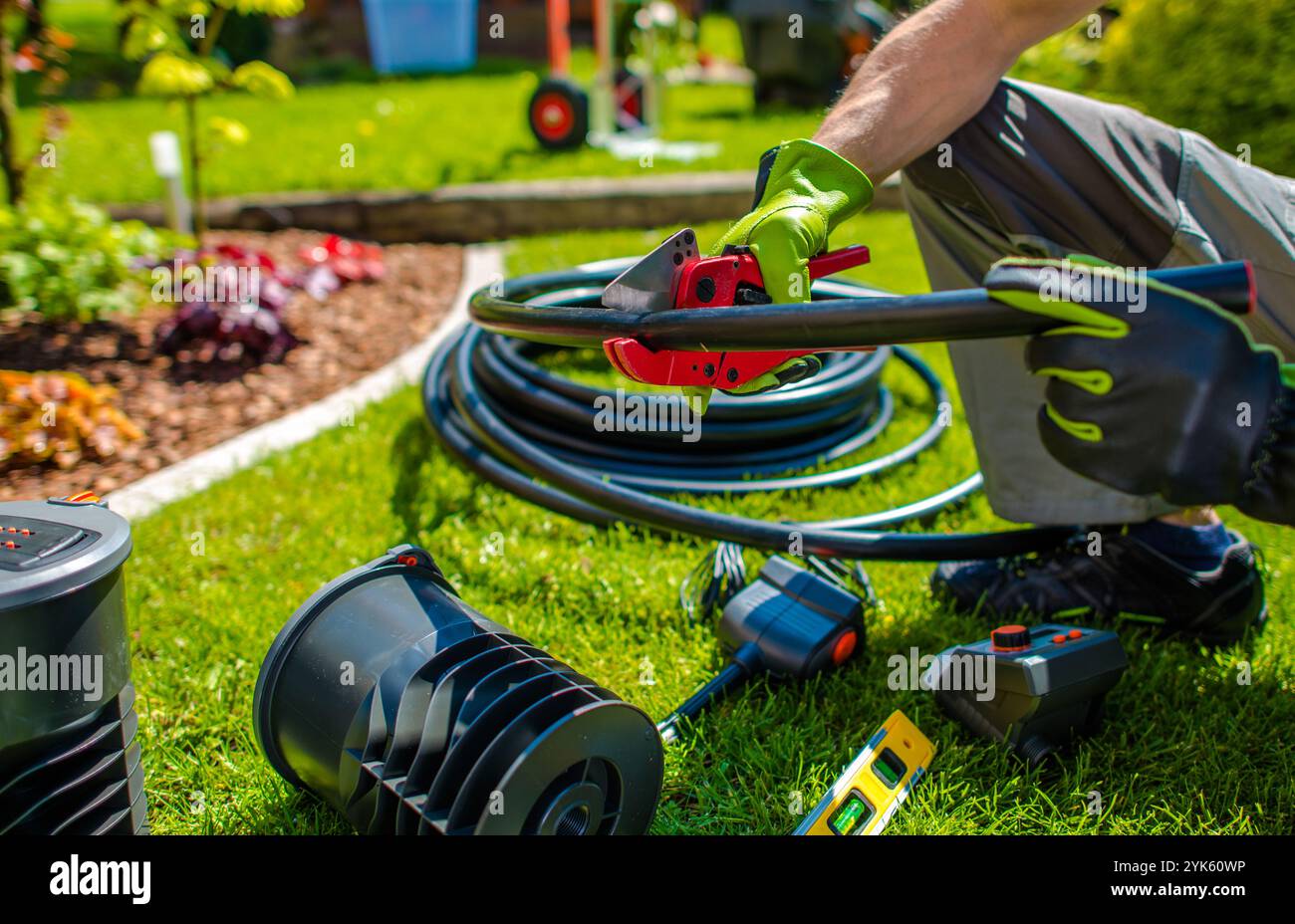 A gardener organizes gardening tools and irrigation system hose on lush ...