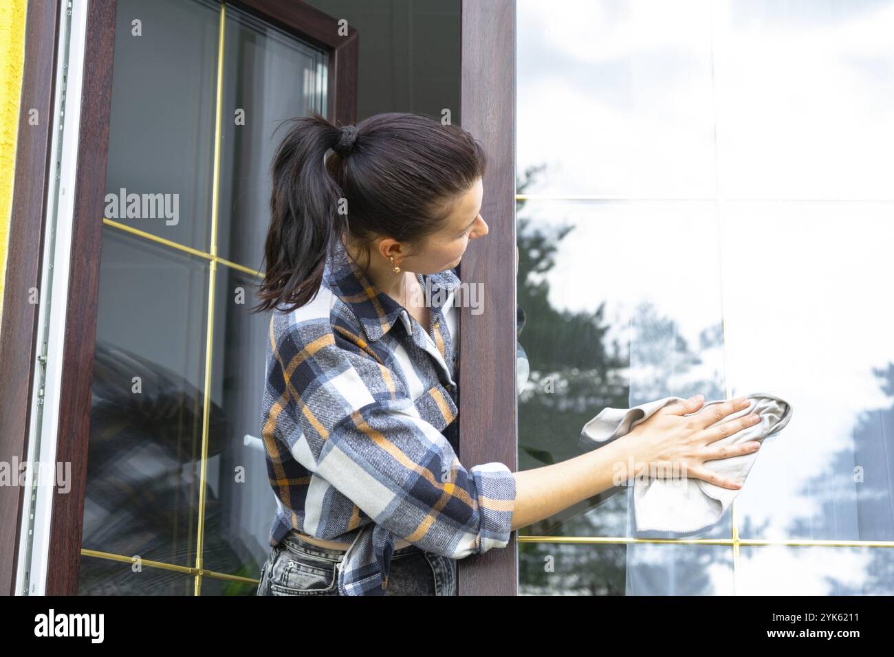 Woman manually washes the window of the house with a rag with spray ...
