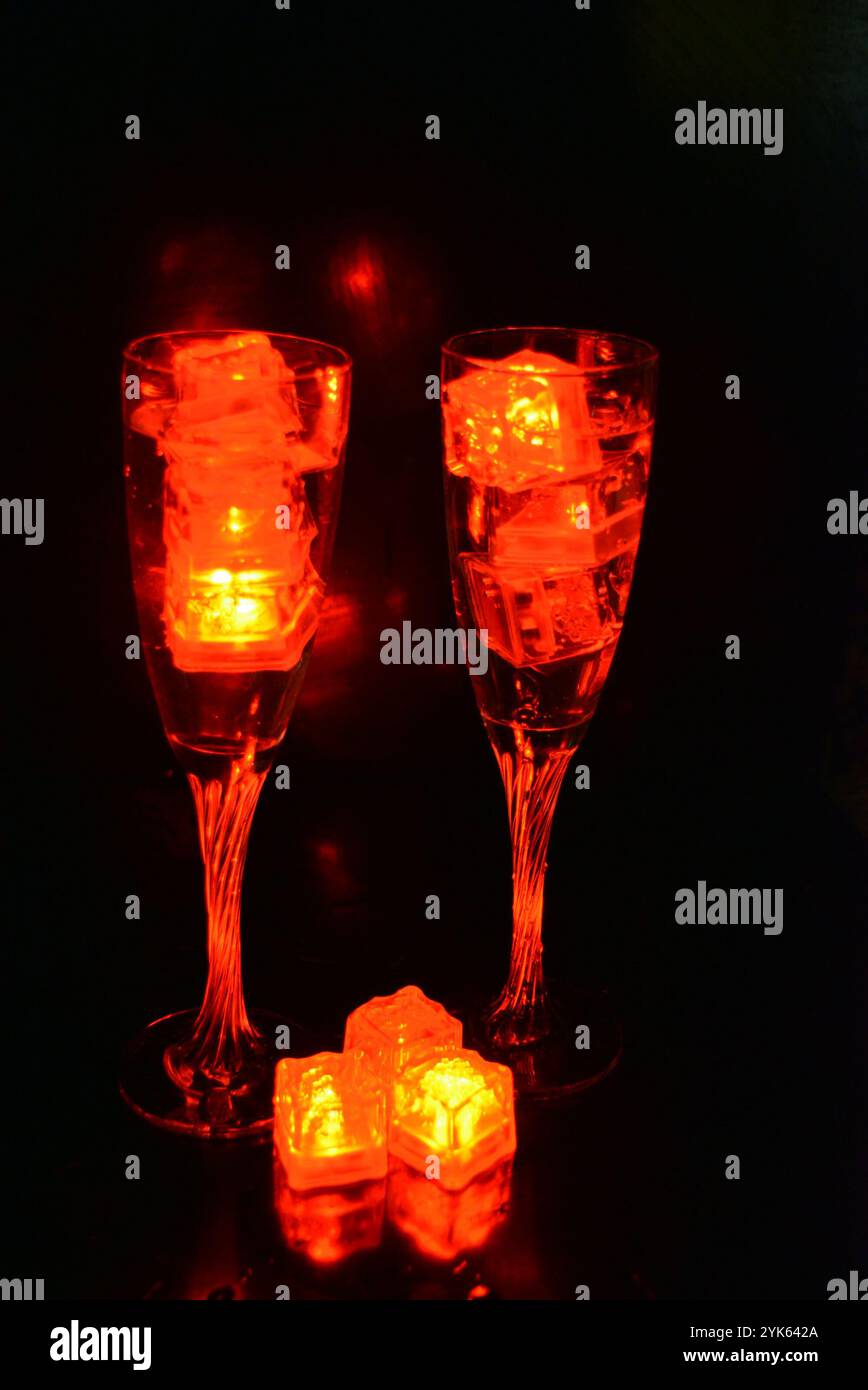 Red glowing ice cubes float in champagne glasses with a drink. Plastic ...