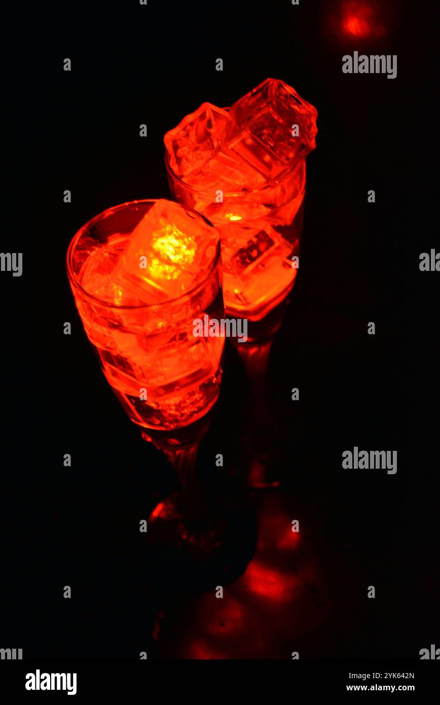 Red glowing ice cubes float in champagne glasses with a drink. Plastic ...