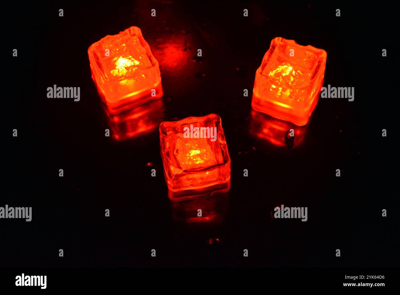 Red glowing ice cubes are located on a black glossy with water drops ...