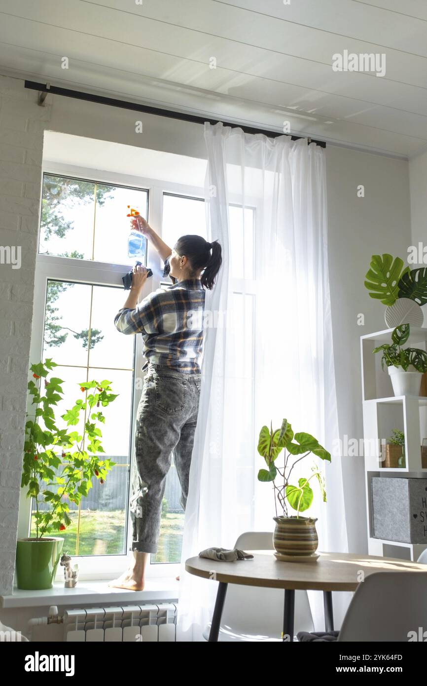Woman manually washes the window of the house with a rag with spray ...