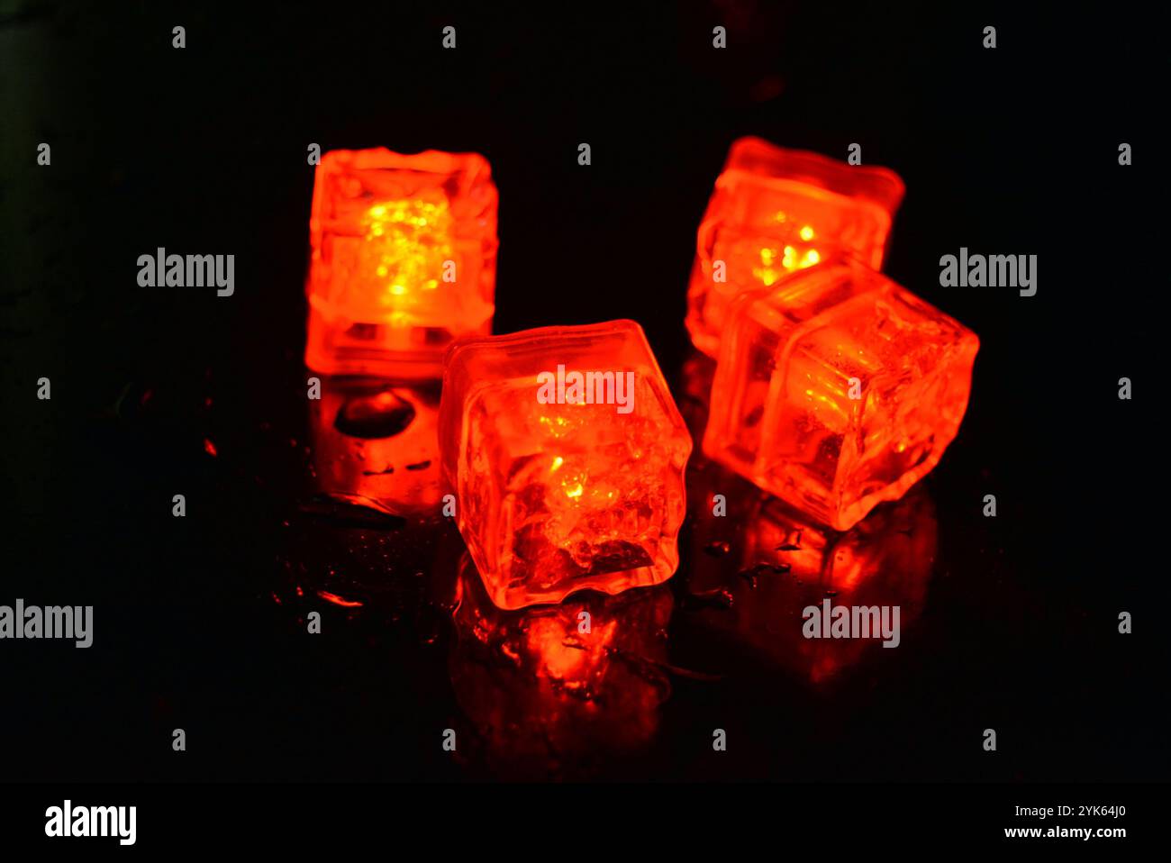 Red glowing ice cubes are located on a black glossy with water drops ...