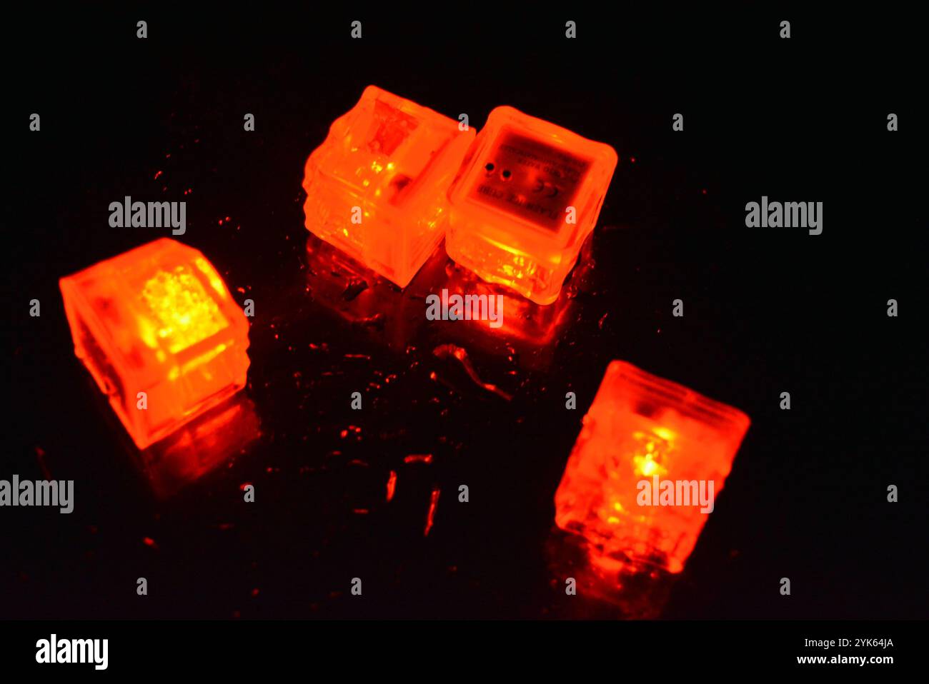 Red glowing ice cubes are located on a black glossy with water drops ...