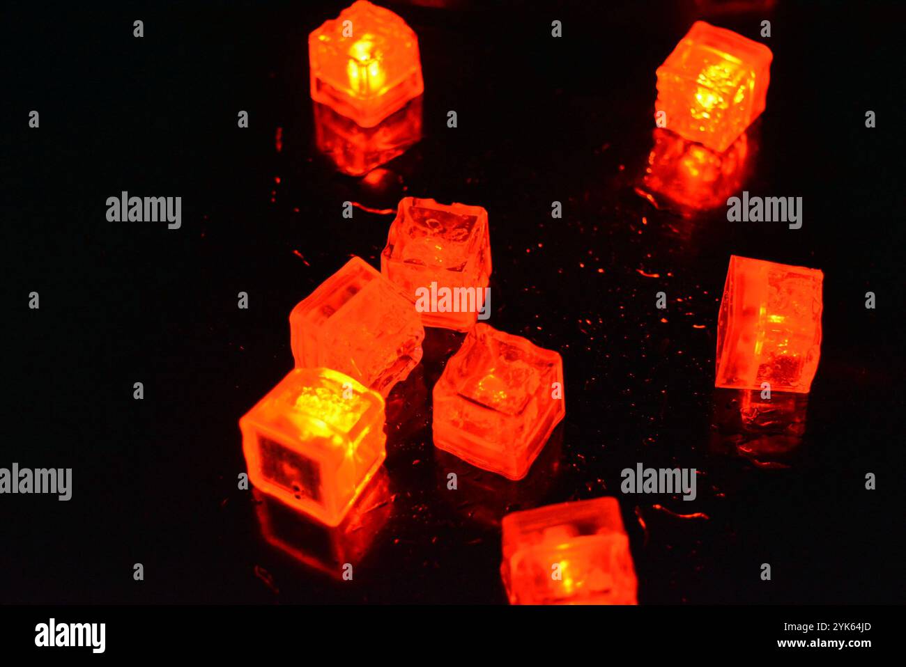 Red glowing ice cubes are located on a black glossy with water drops ...