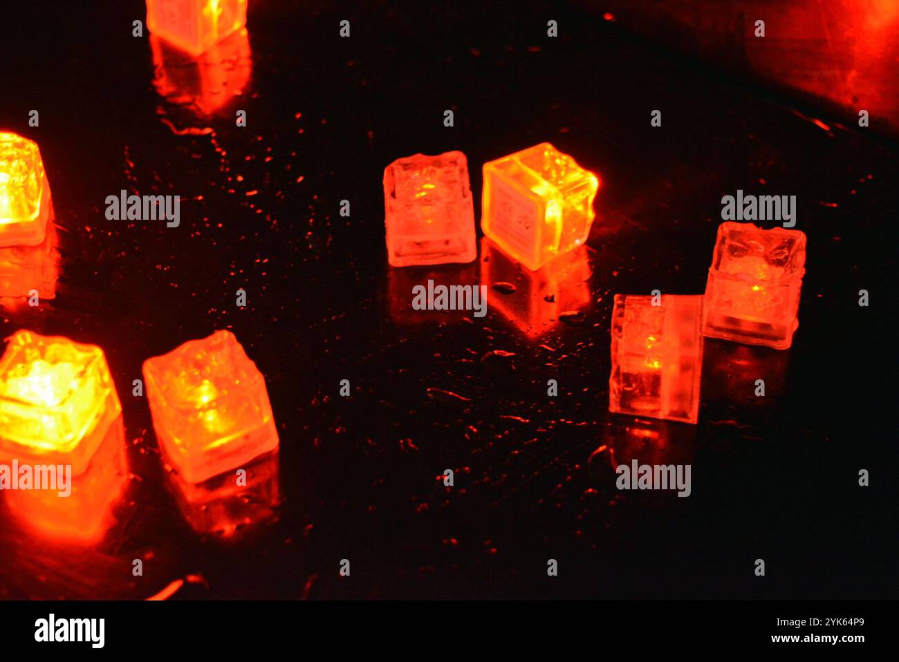 Red glowing ice cubes are located on a black glossy with water drops ...