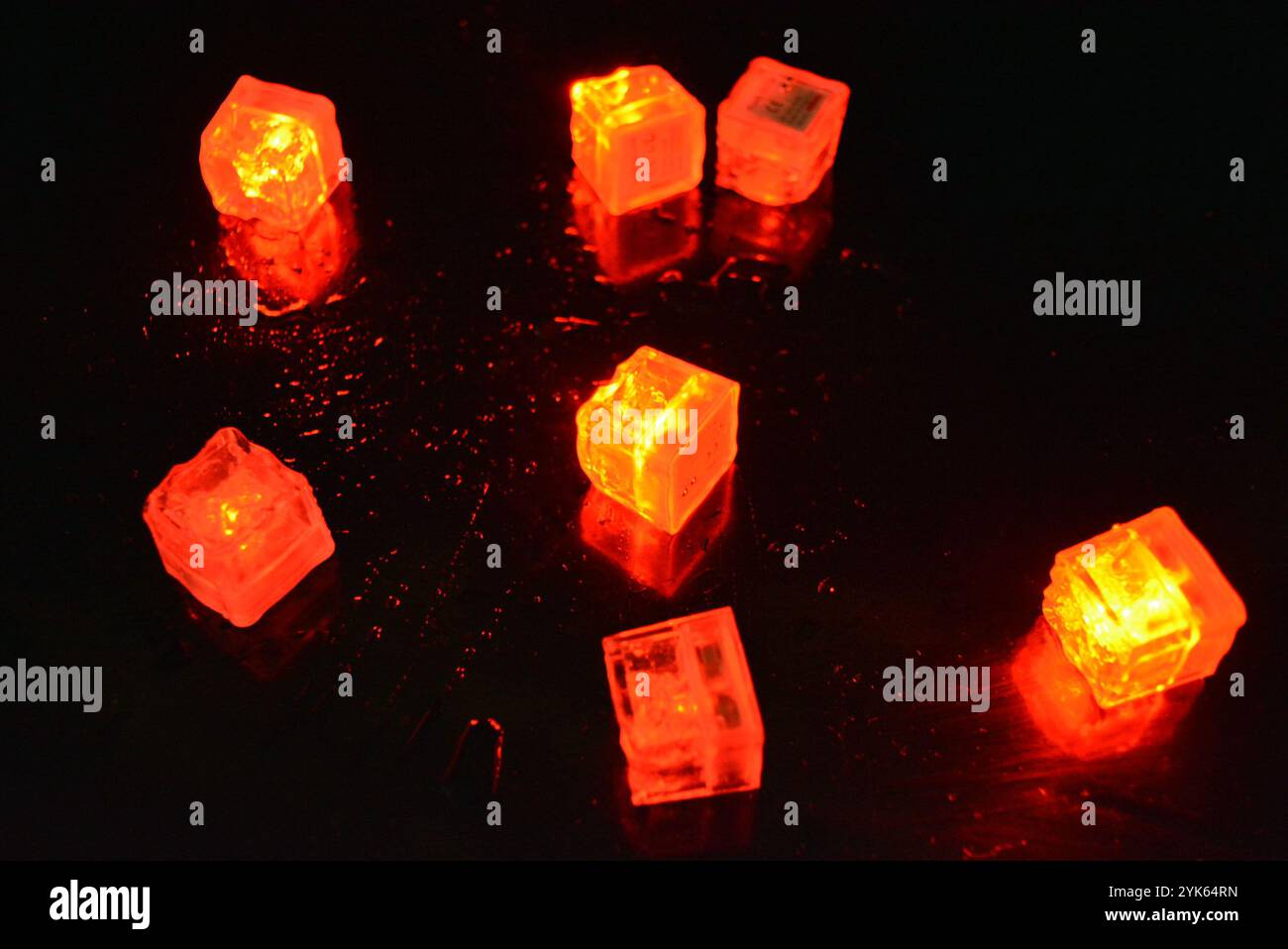 Red glowing ice cubes are located on a black glossy with water drops ...