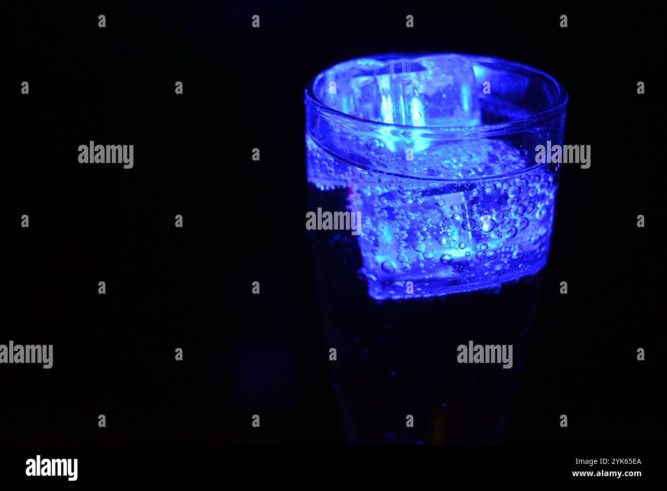 Beautiful and bright blue glowing ice cube floats in a glass champagne ...