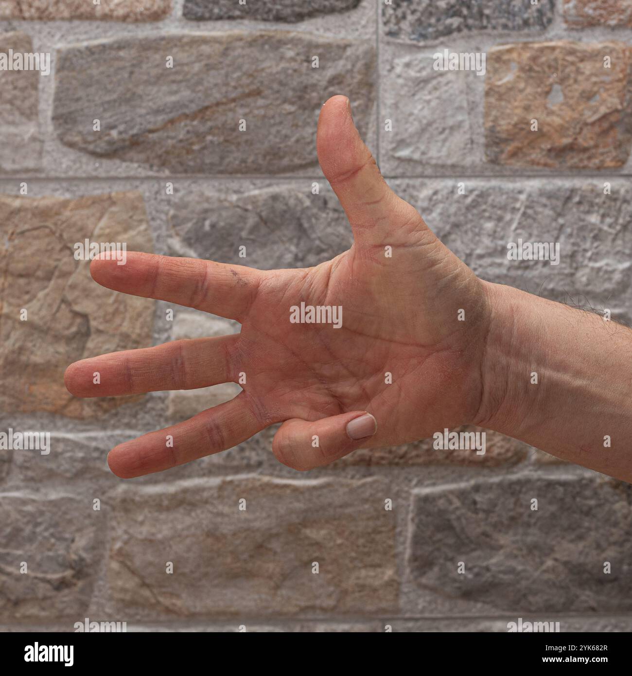 Hand showing four fingers extended against a textured stone wall ...