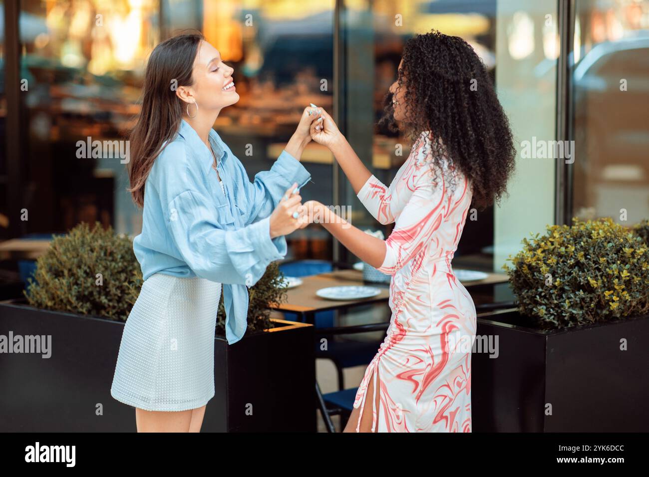 Two friends dancing joyfully outside a trendy cafe on a sunny day Stock ...