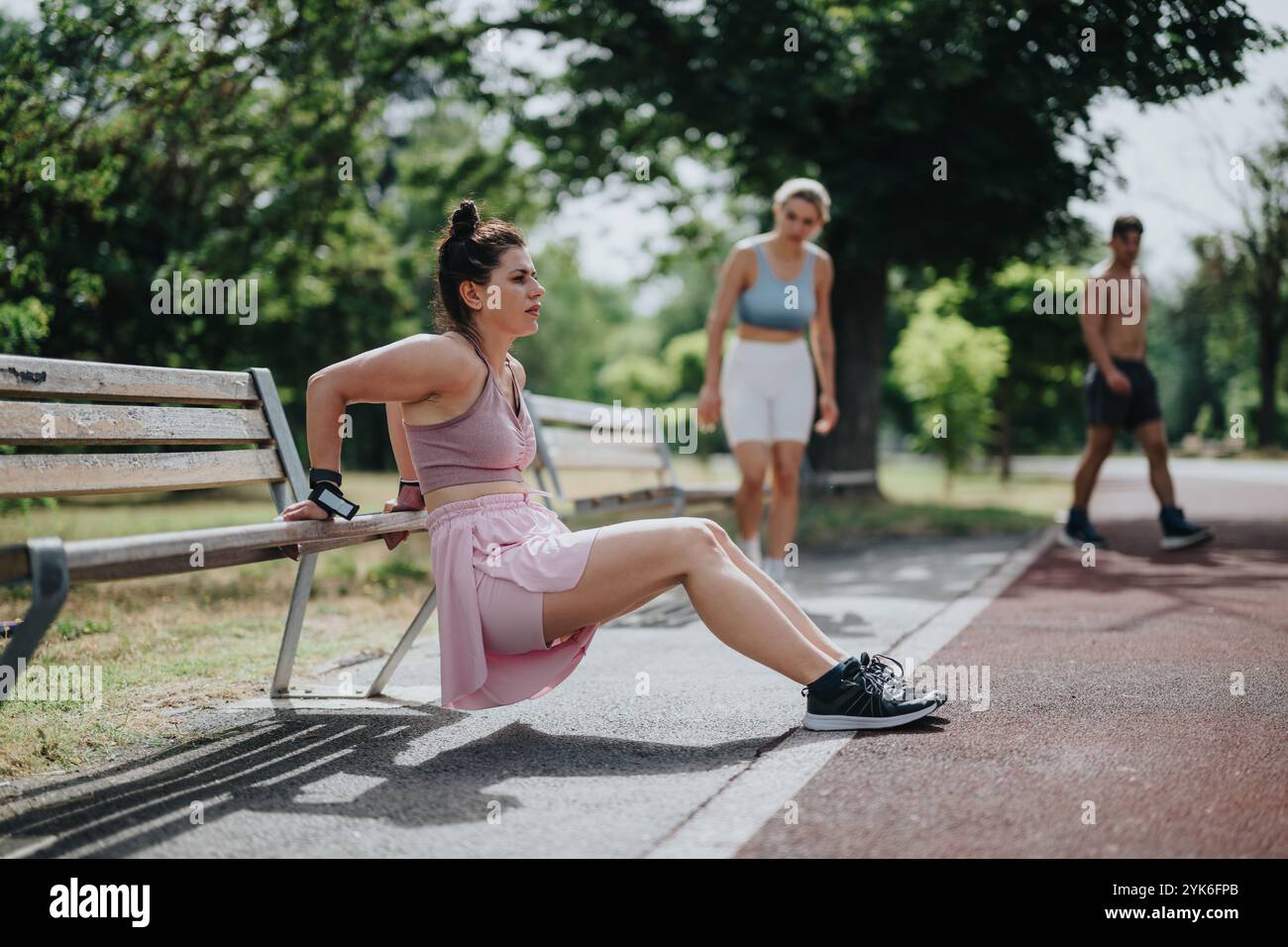 Woman exercising on park bench with friends during outdoor workout ...