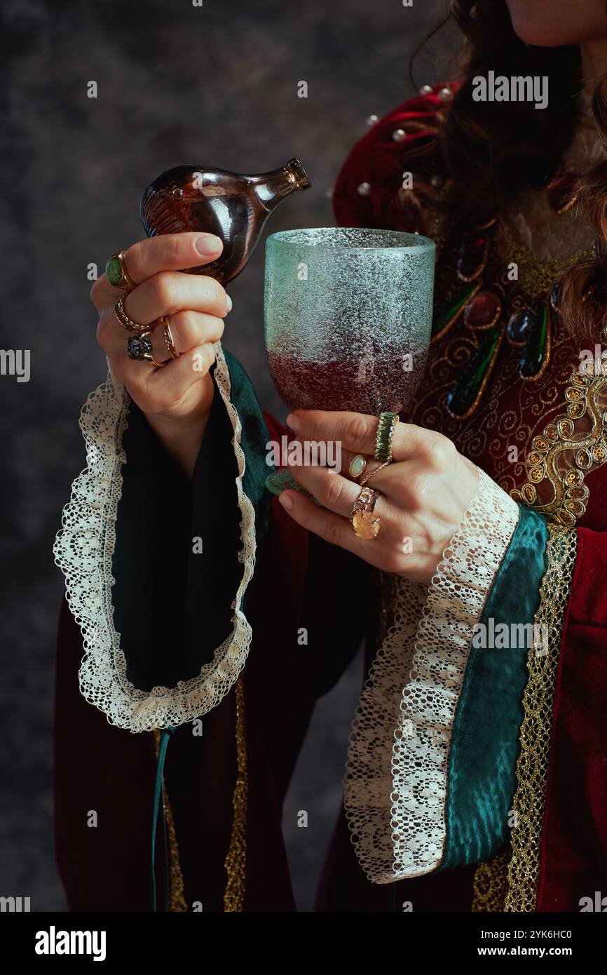 Closeup on medieval queen in red dress pouring poison into the goblet ...