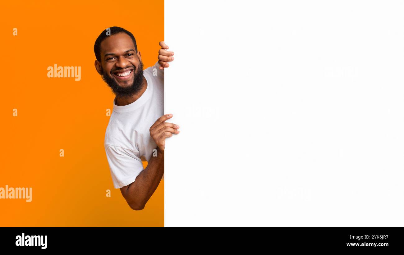Black man peeking out blank white advertising billboard at studio Stock ...