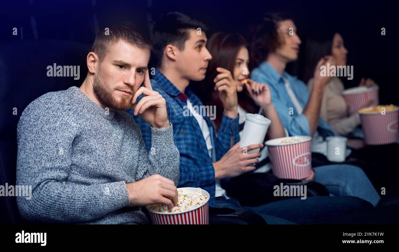 Dull movie. Bored man with company of people in cinema Stock Photo - Alamy