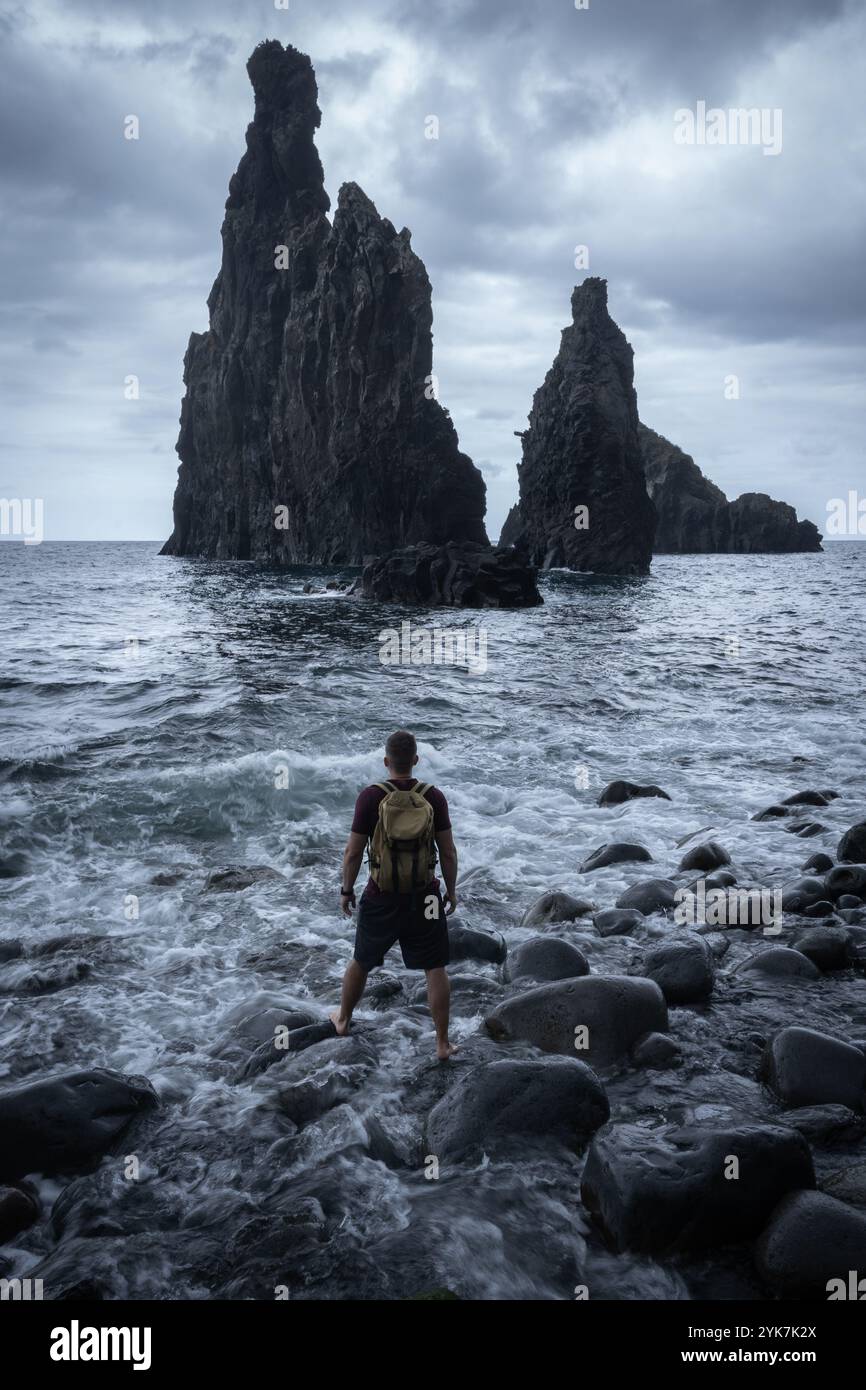 Man on the beach looking towards big towering sea stacks, vertical shot ...