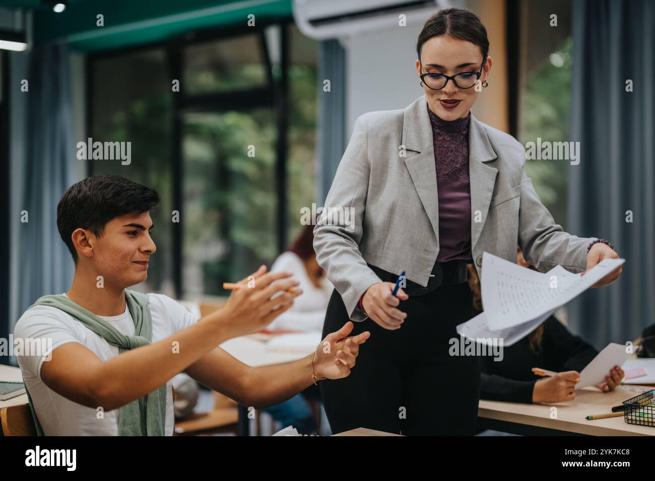 Teacher assisting student with assignment in modern classroom Stock Photo - Alamy