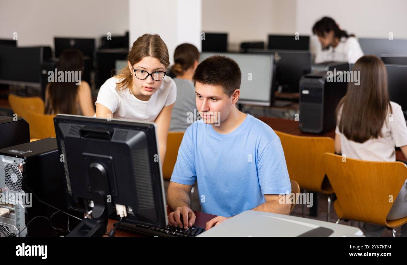 Clever female teenager helping to the male classmate while he is ...