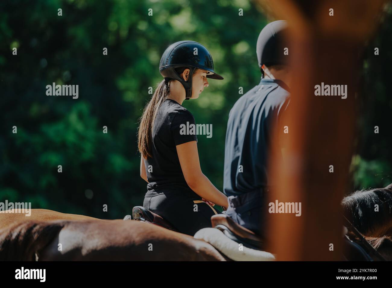 Two young equestrians riding horses in a lush green forest setting ...