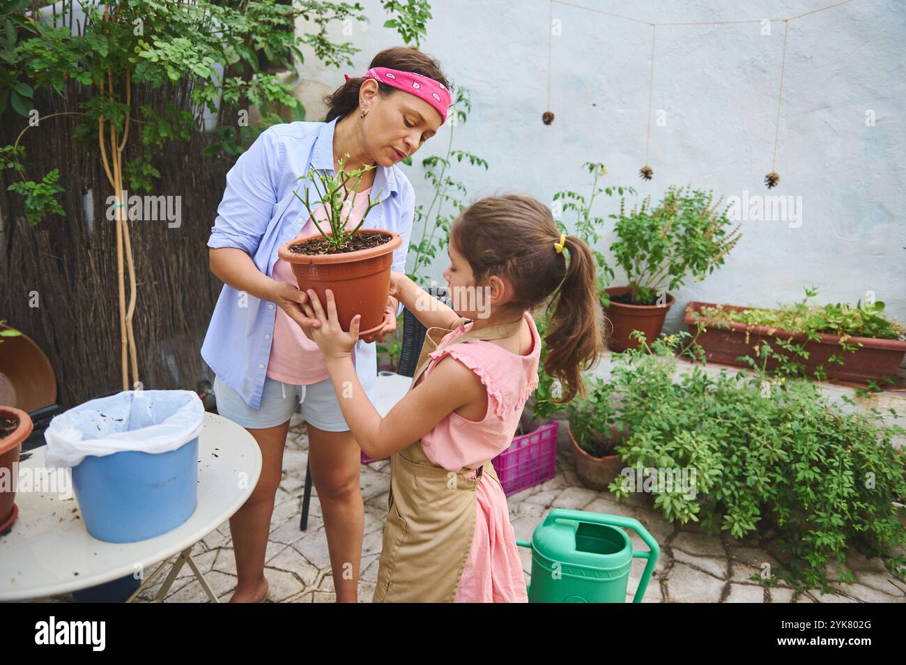 A mother and daughter engage in gardening, holding a potted plant in a ...