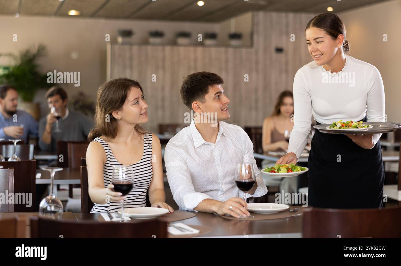 Waitress brings order to young man and woman couple Stock Photo - Alamy