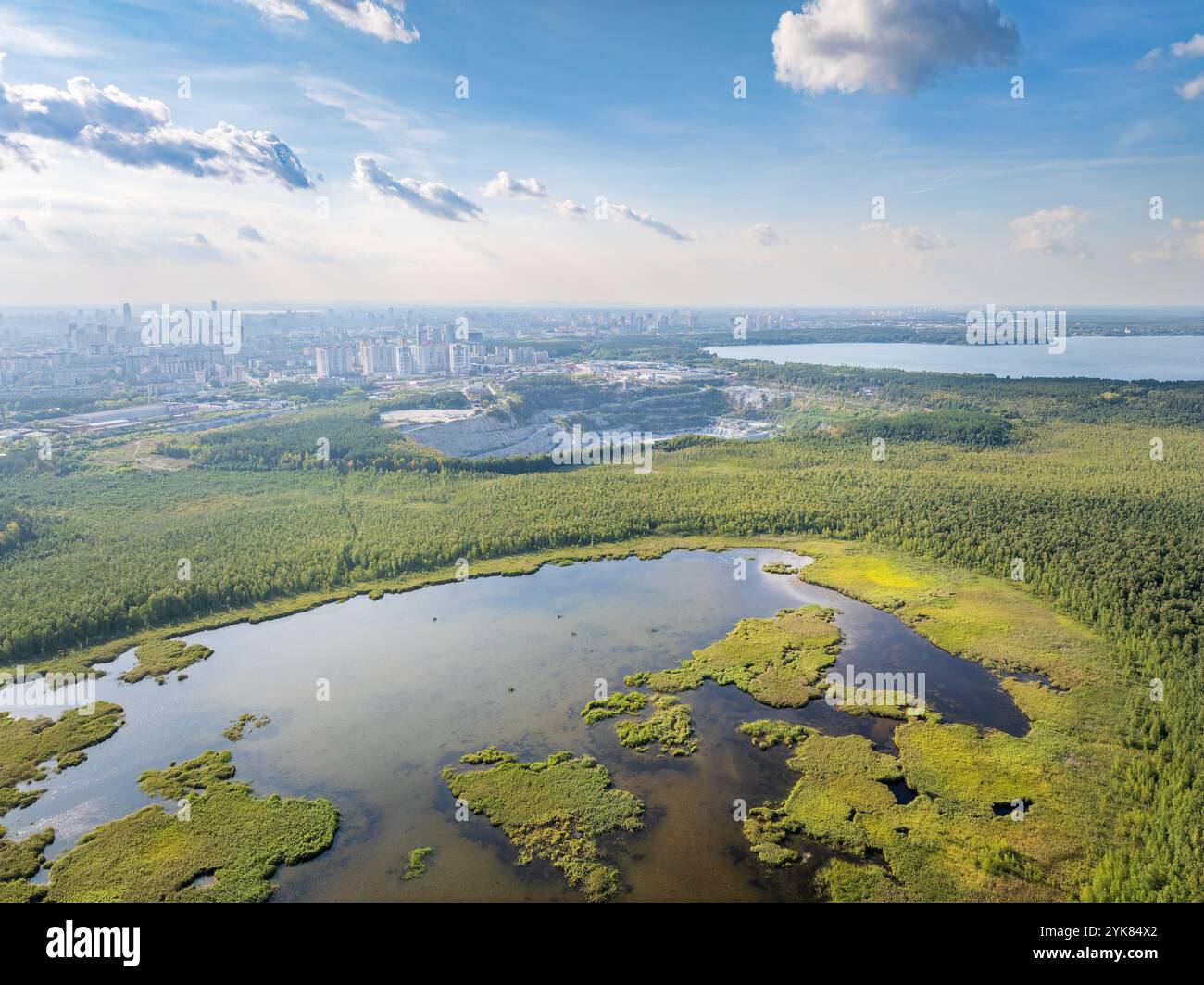 Big lake with green shores in bright sun light and city on horizon ...