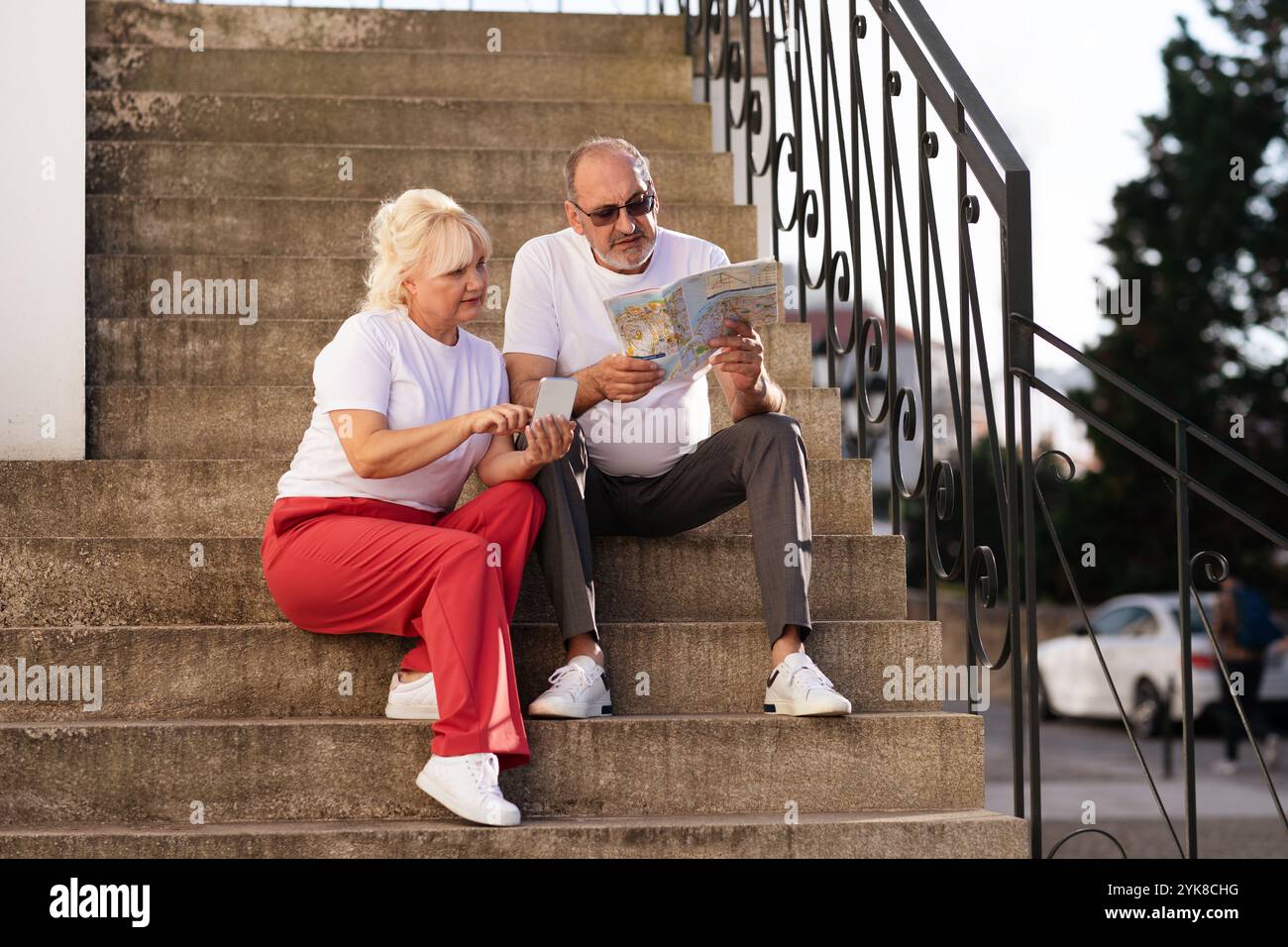 Happy couple exploring a map while sitting on city steps in summer ...