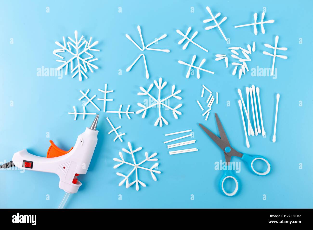 DIY cotton swab snowflake decorations in progress on blue background with hot glue gun, scissors ...