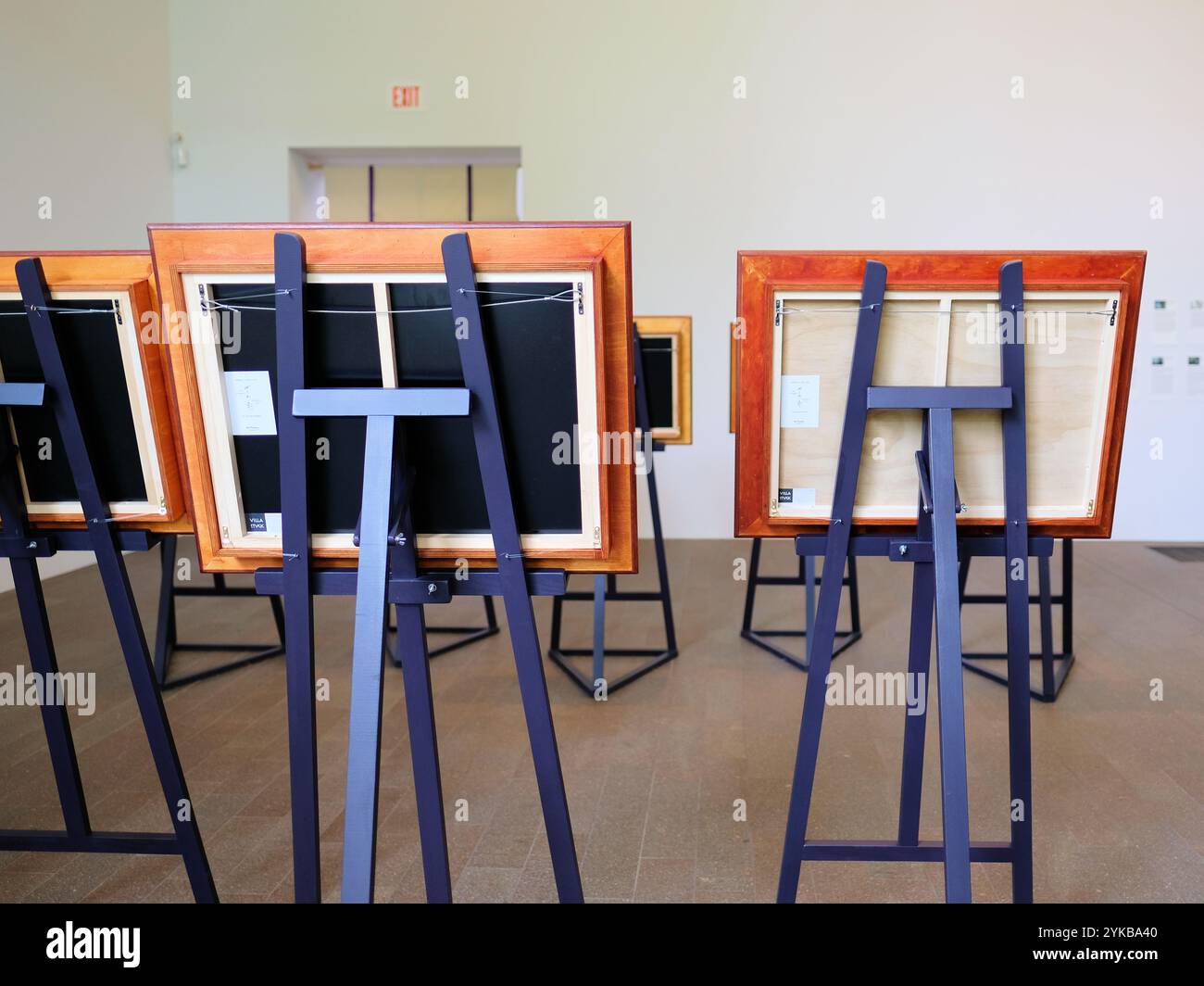 Wooden easels at a museum art exhibit seen from behind; rear view of ...