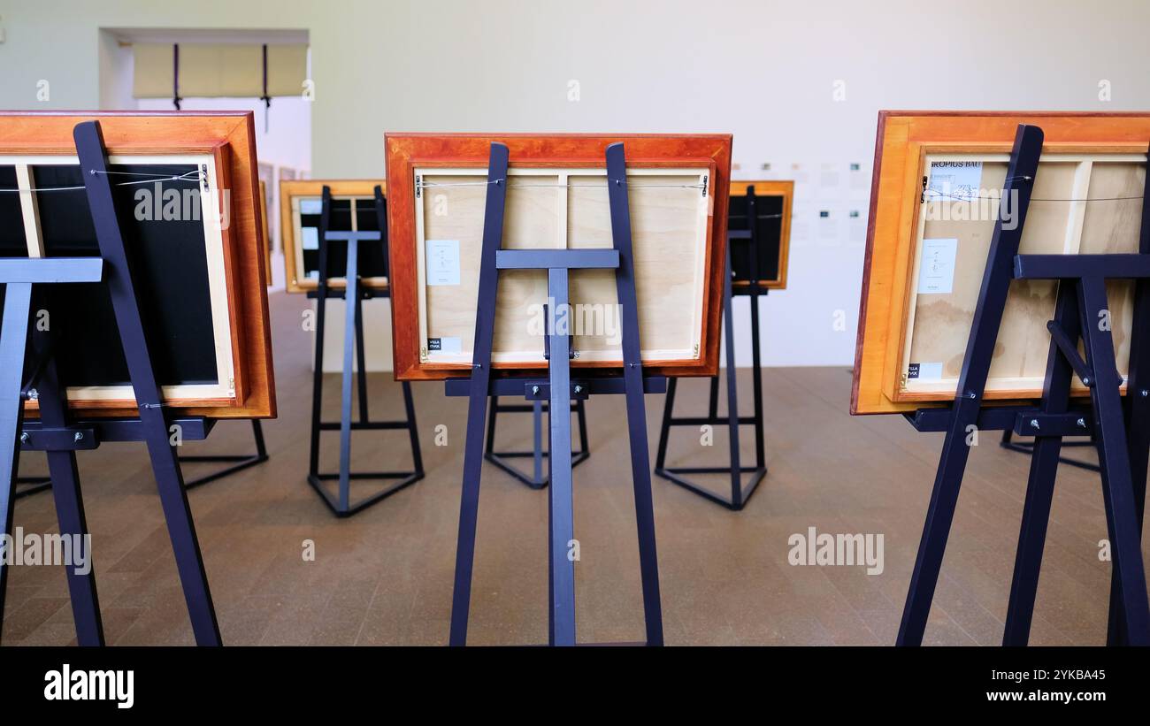 Wooden easels at a museum art exhibit seen from behind; rear view of ...